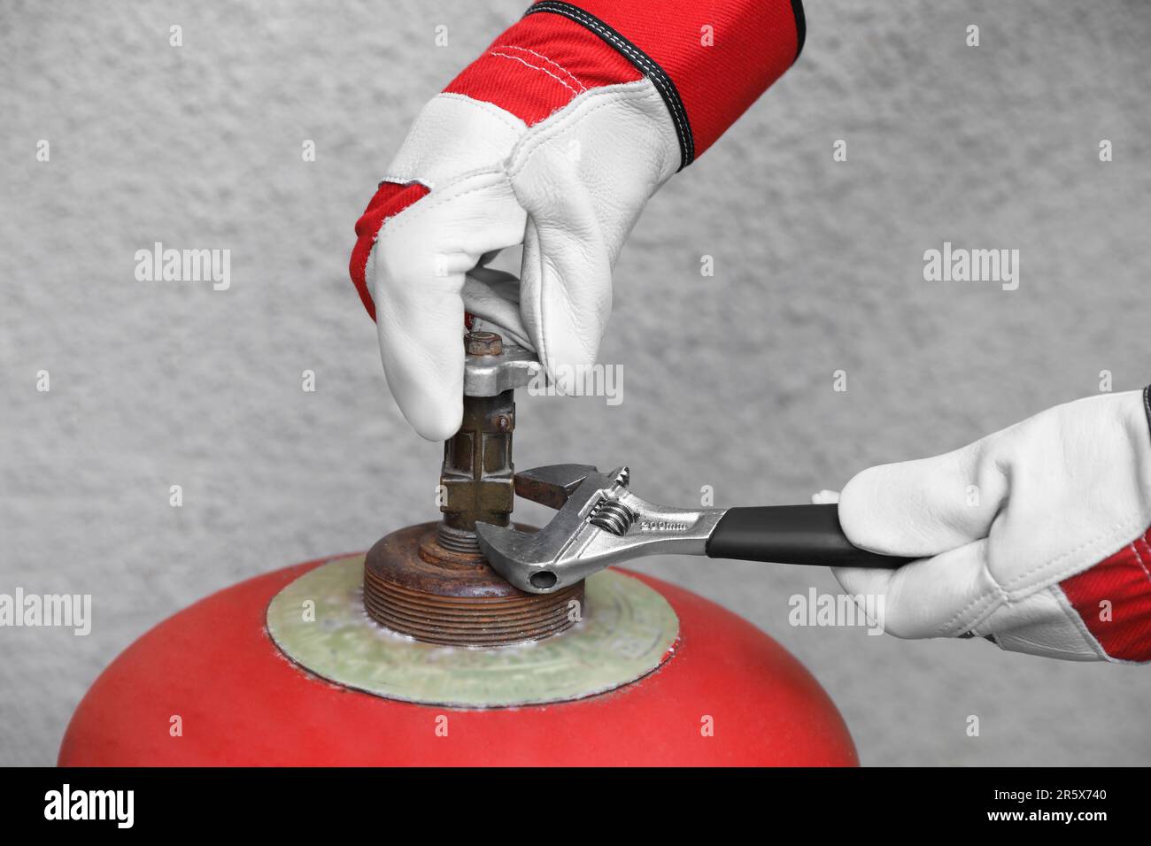 Worker with adjustable wrench opening red gas cylinder near wall ...