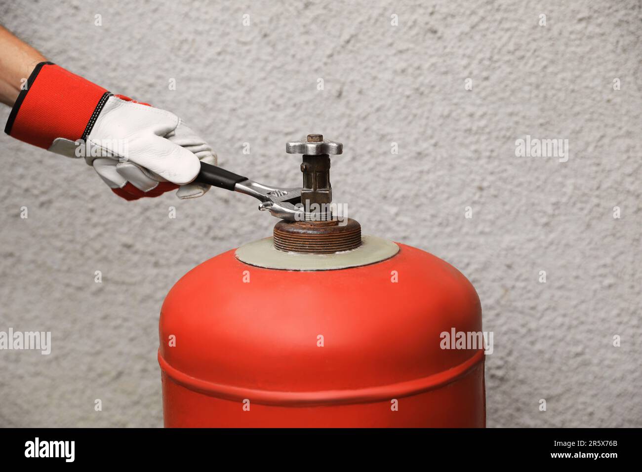 Worker with adjustable wrench opening red gas cylinder near wall ...