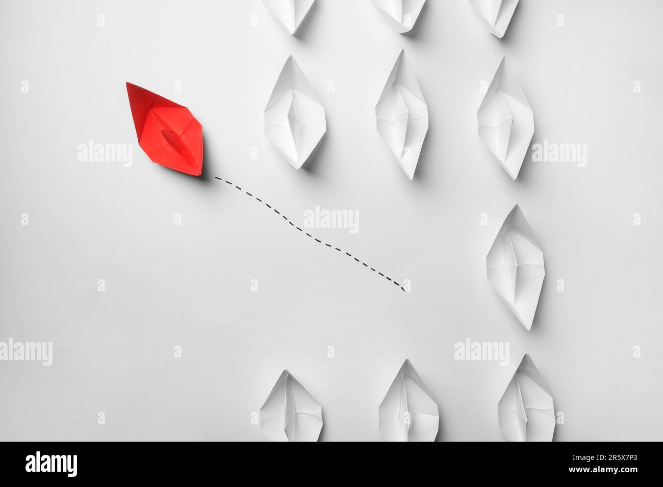 Red paper boat floating away from others on white background, flat lay ...