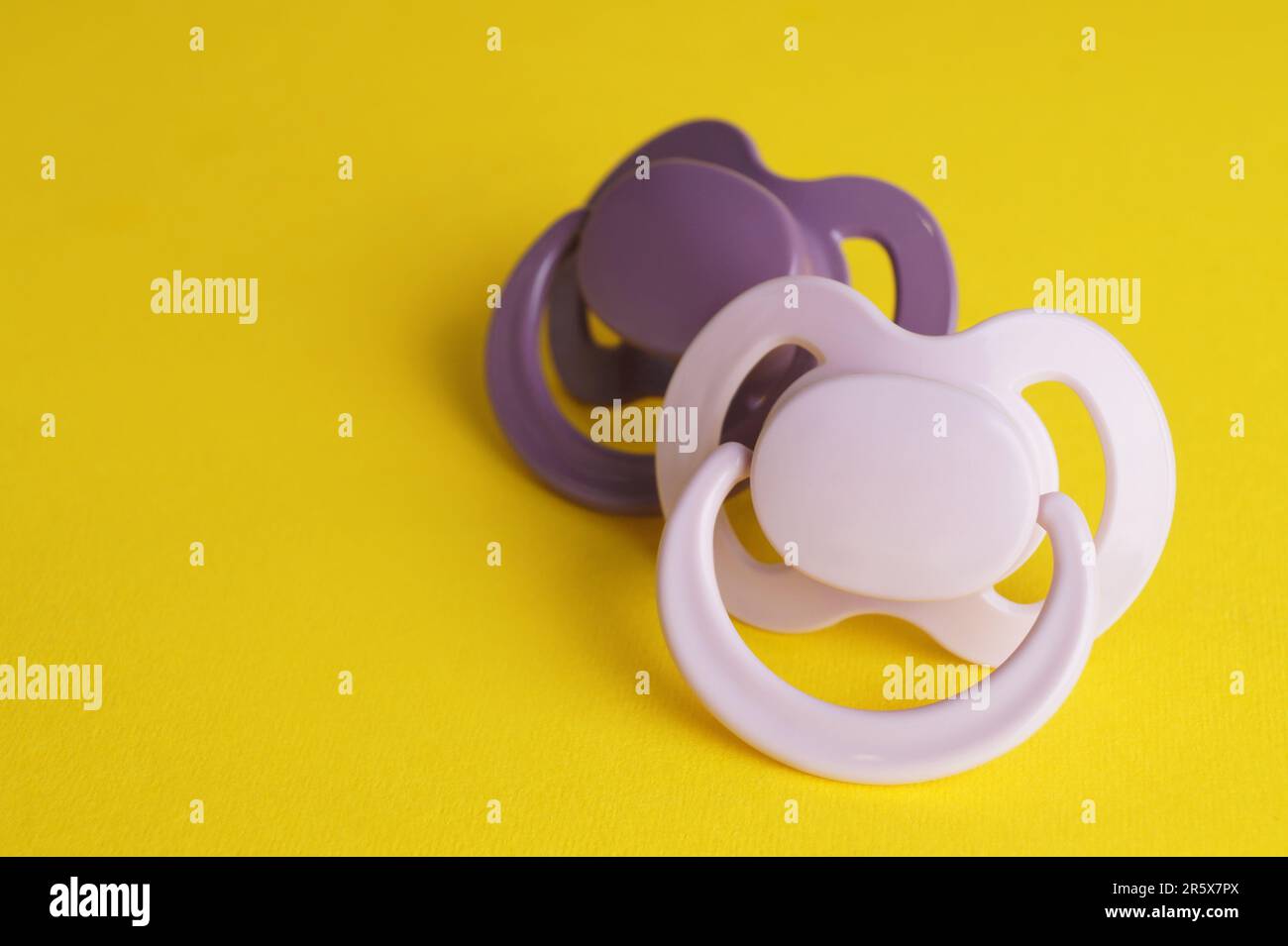 New baby pacifiers on yellow background. Space for text Stock Photo - Alamy