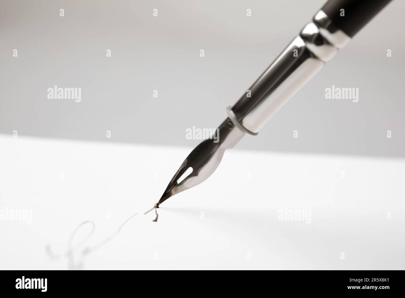 Signing on sheet of paper with fountain pen against light grey ...