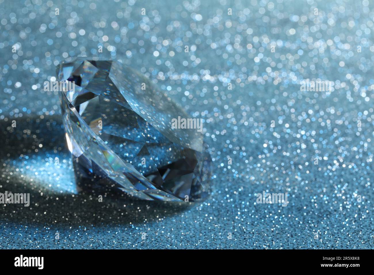 Beautiful dazzling diamond on blue glitter background, closeup. Space ...