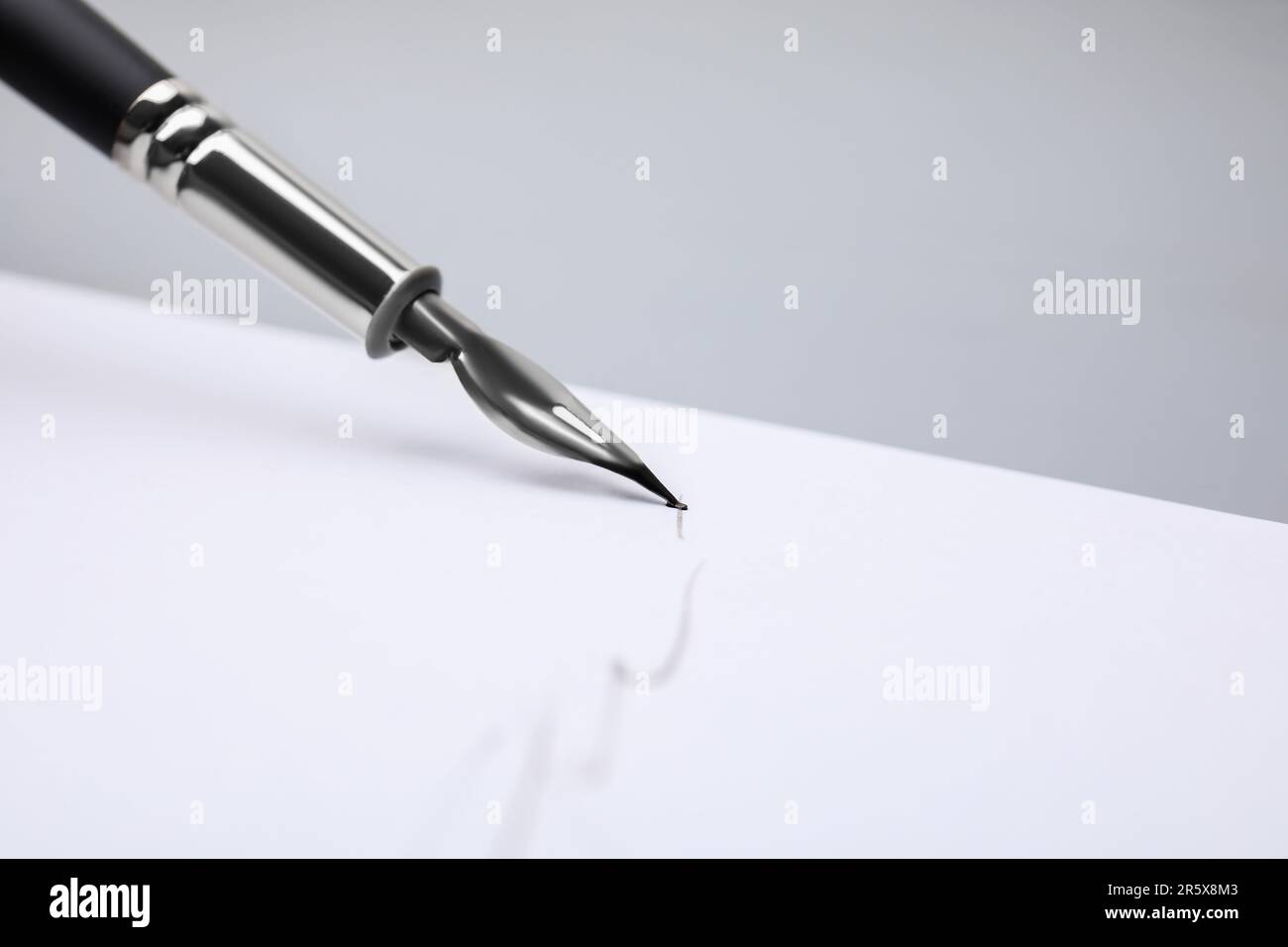 Signing on sheet of paper with fountain pen against light grey ...