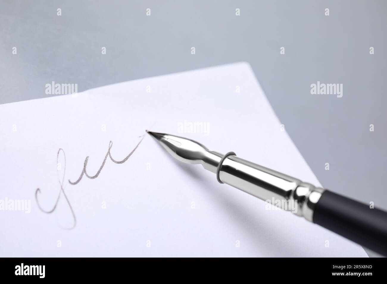 Signing on sheet of paper with fountain pen against light grey ...