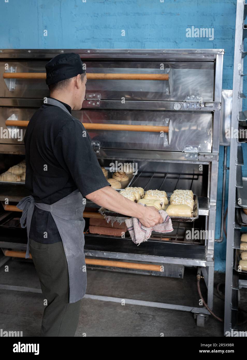 A young Hispanic baker is putting a tray full of sweet breads inside ...