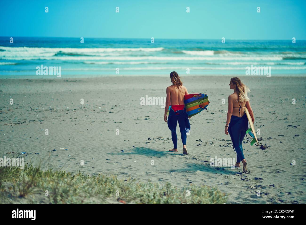 Get on your board and surf. a young couple walking on the beach with ...