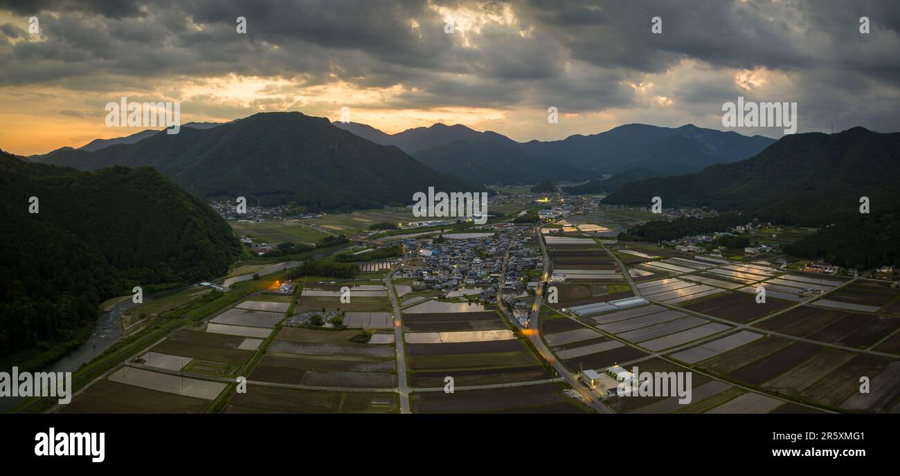 Dramatic sunset sky over small farming village and flooded rice fields ...