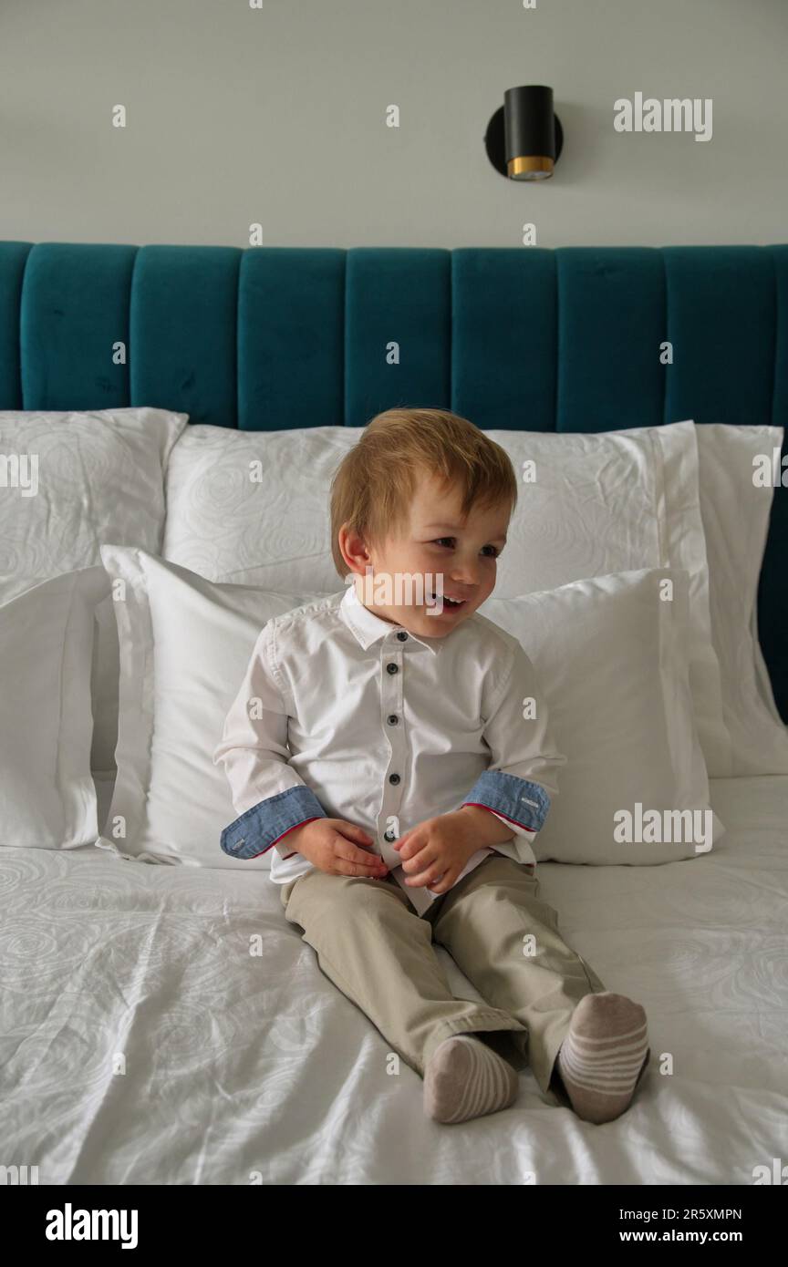 Little boy dressed for celebration sitting on a bed Stock Photo - Alamy