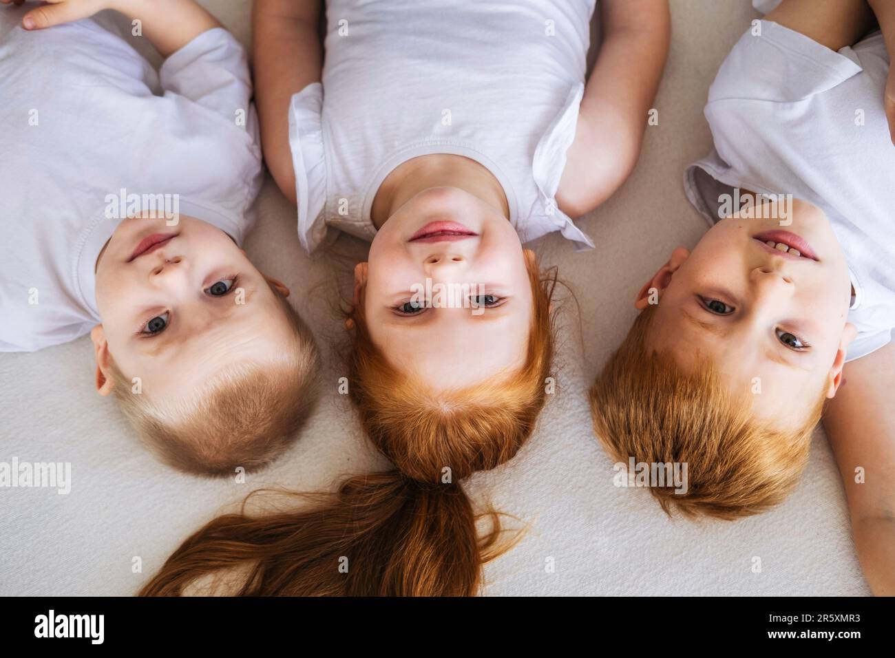 Redhaired children lie on bed with white linens. Brothers and sister ...