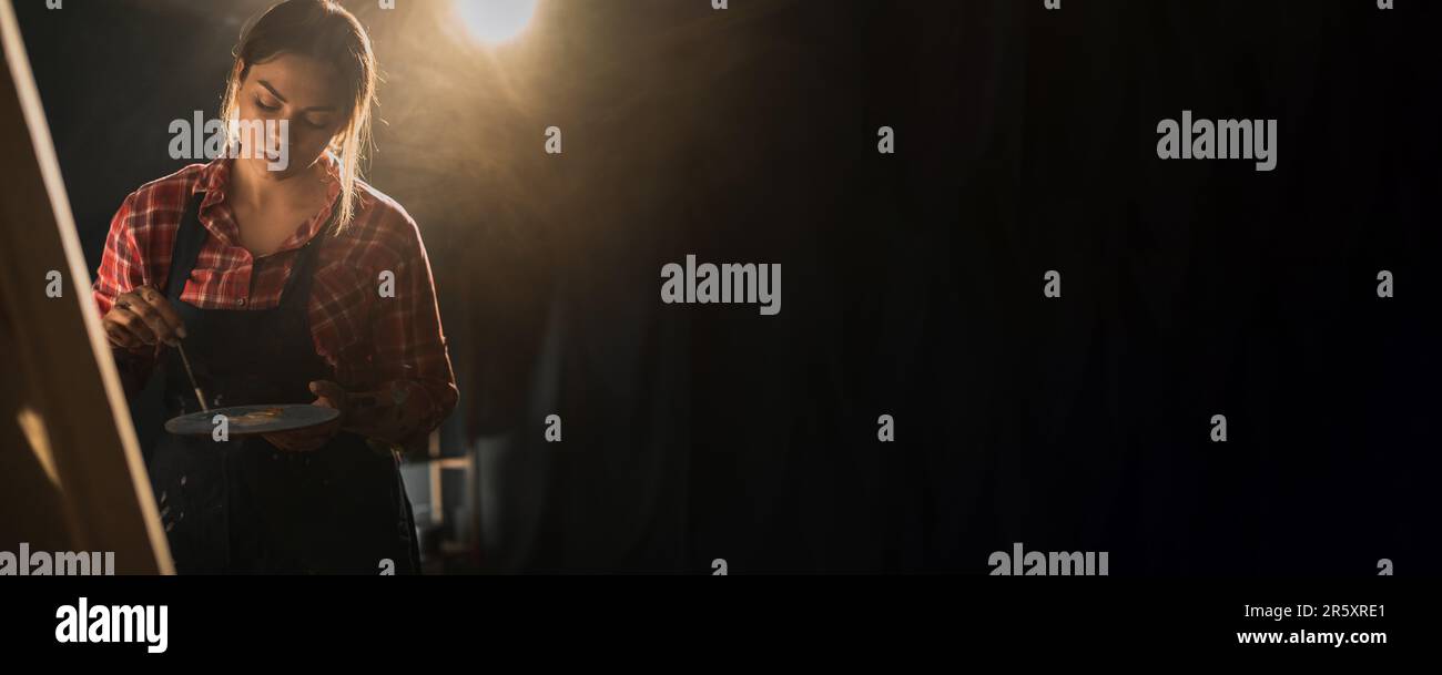 Beautiful female painter in dark art studio. Young talented artist ...