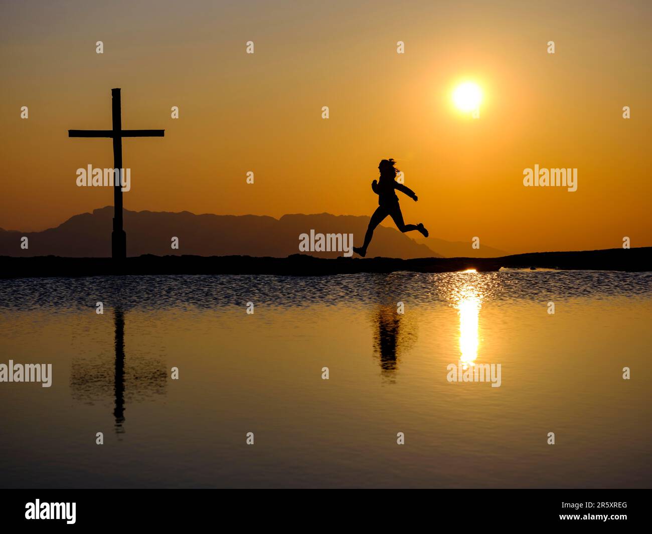 Silhouette of a runner with summit cross at sunset, reflection in the ...
