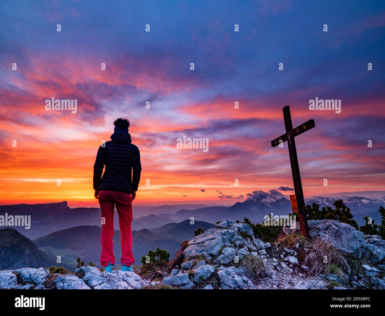 Mountaineer next to the summit cross of the iceberg and red clouds at ...