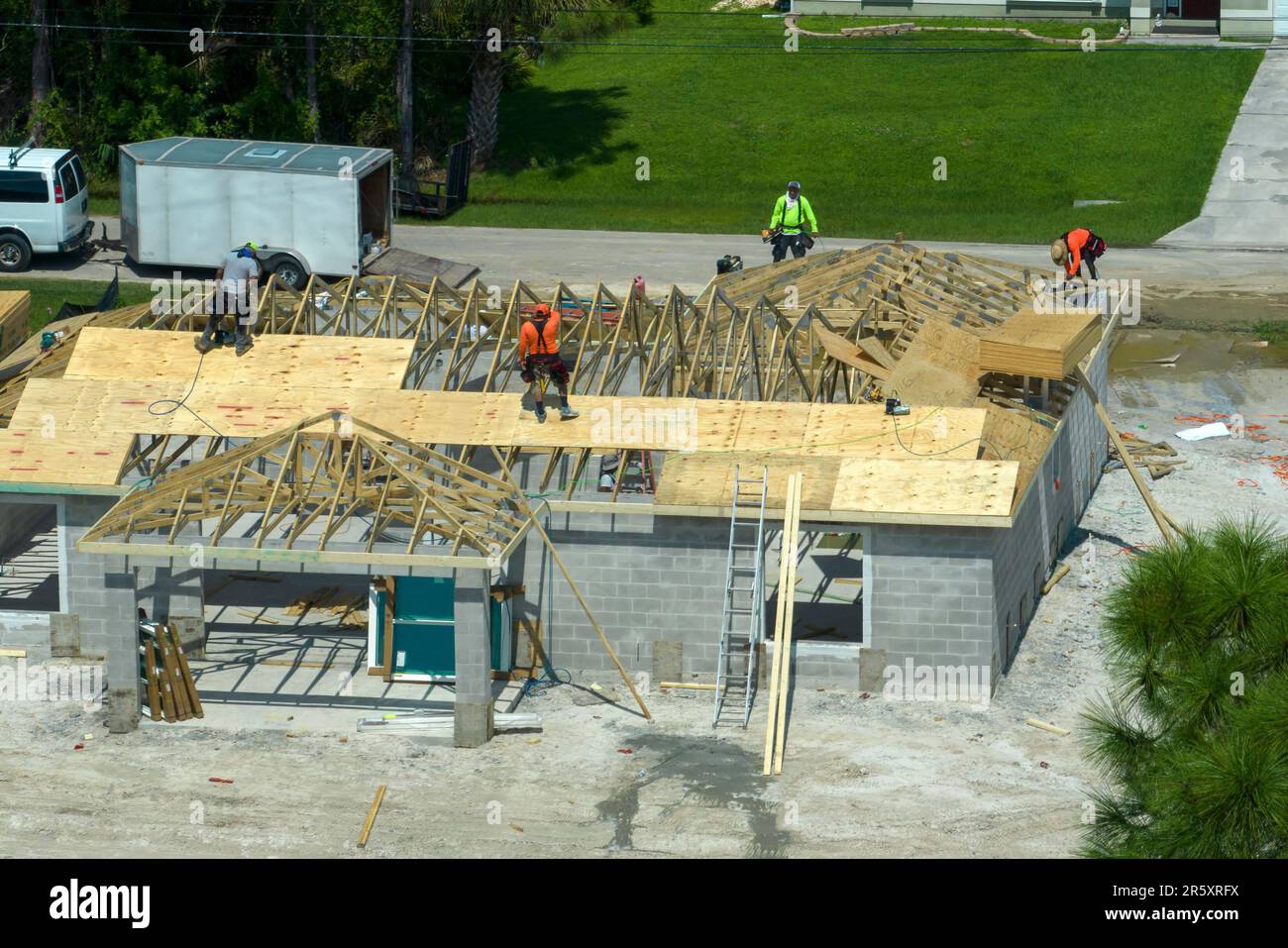 Aerial view of builders working on unfinished residential house with wooden roof frame structure ...
