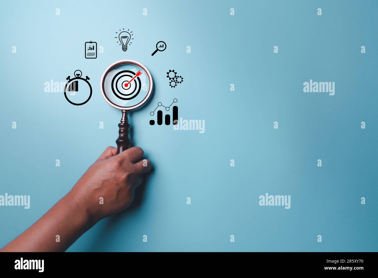 Hand holding target board inside vintage magnifying glass for focus business objective on blue ...