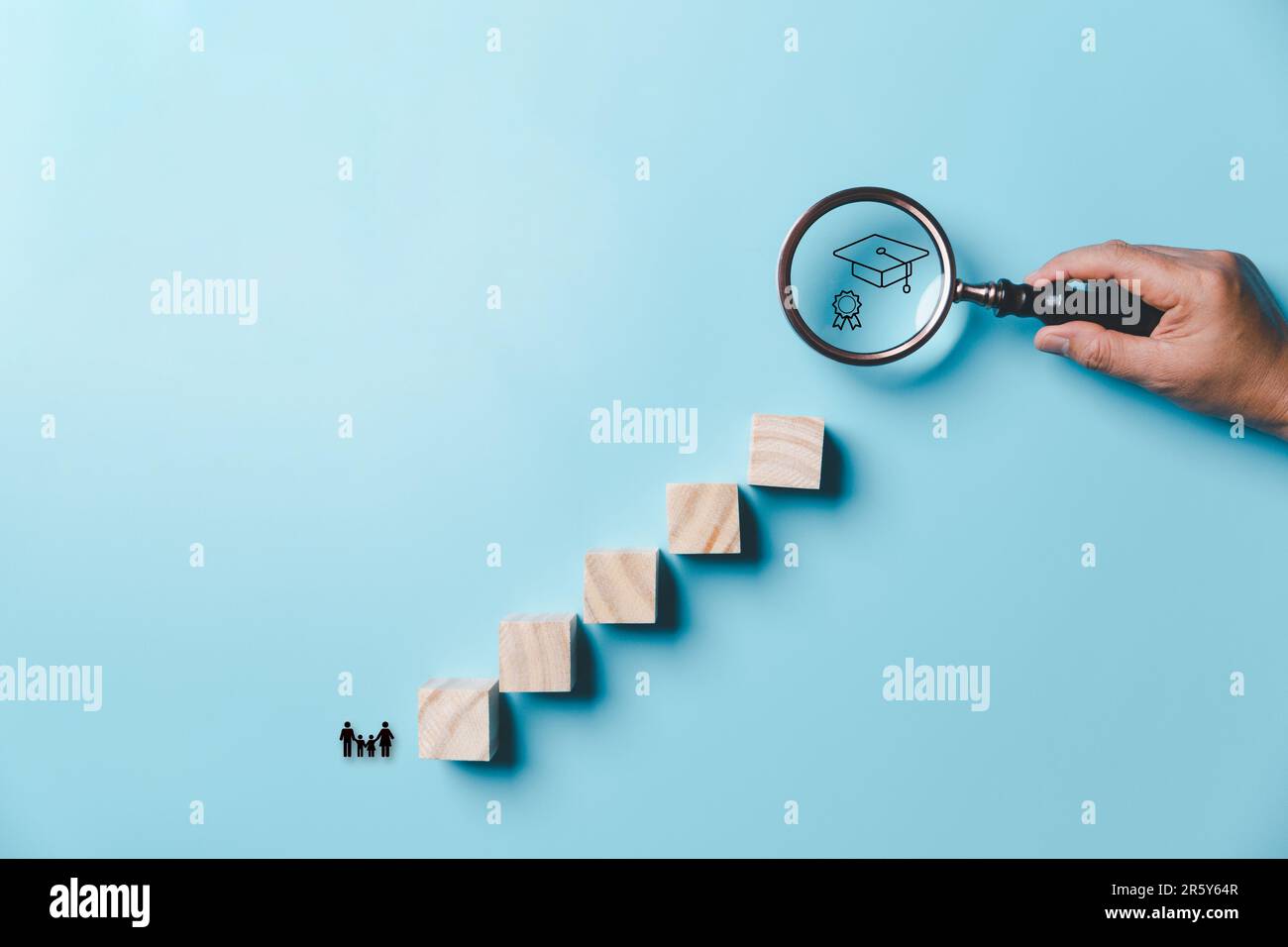 Hand holding a magnifying glass with education icons on a blue ...