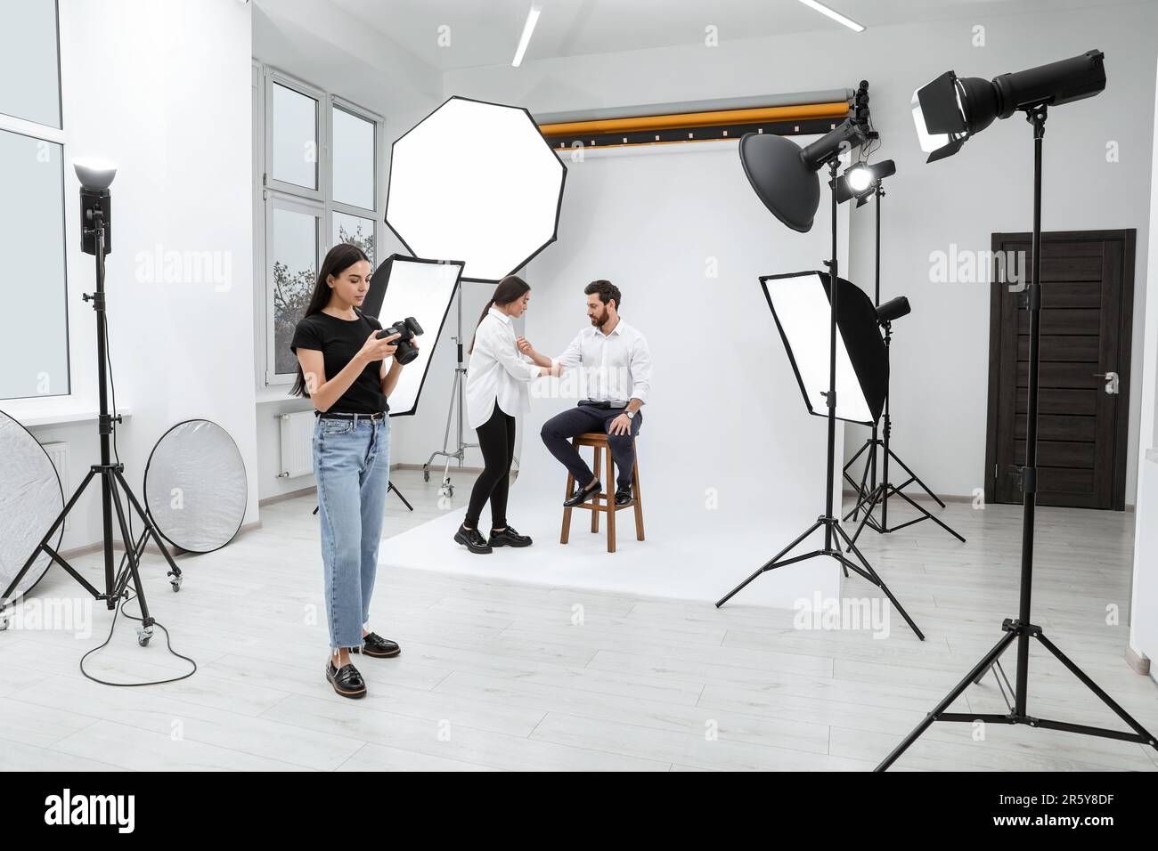 Professional photographer and stylist working with model in modern ...