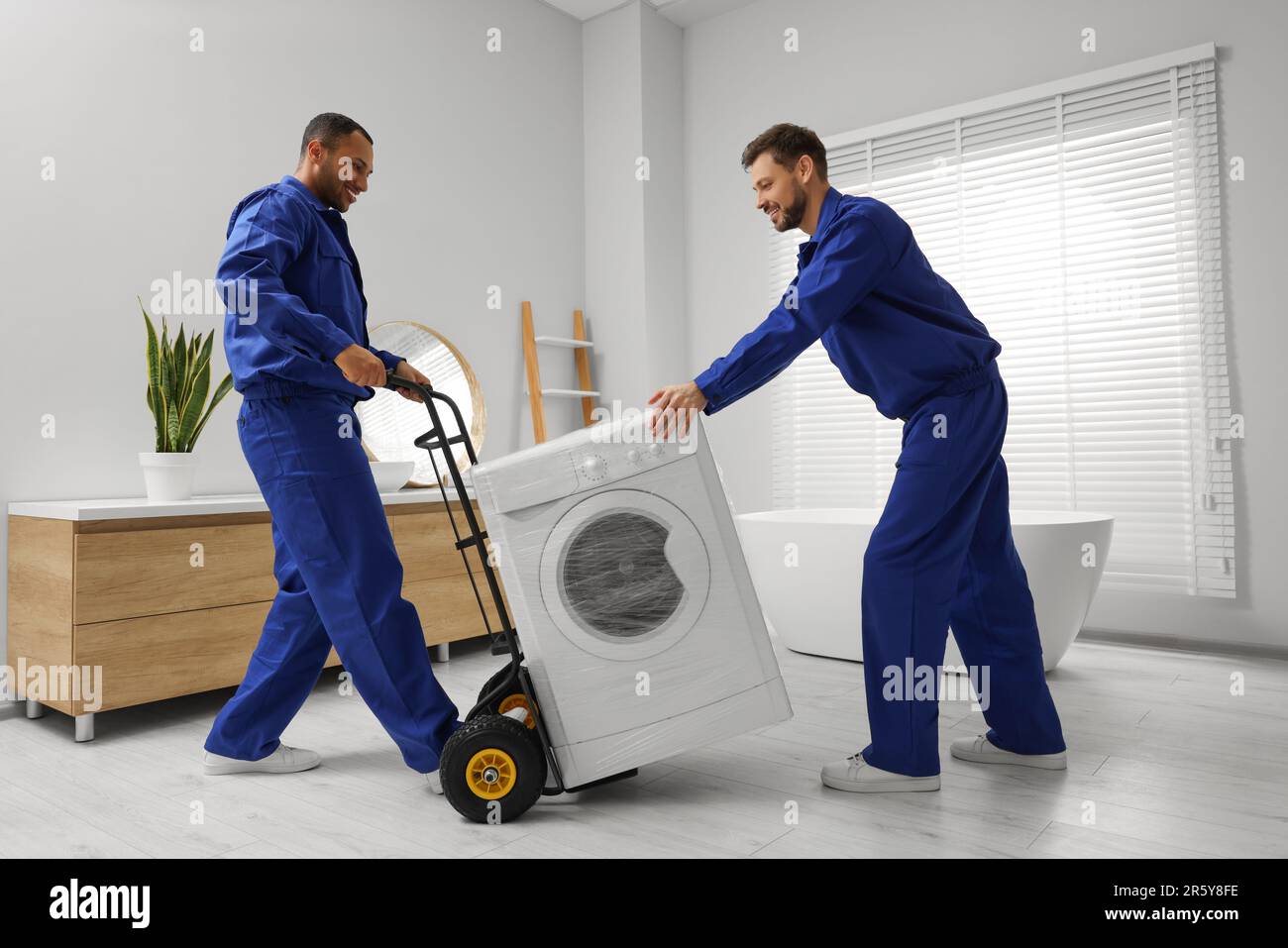 Male movers carrying washing machine in bathroom. New house Stock Photo ...