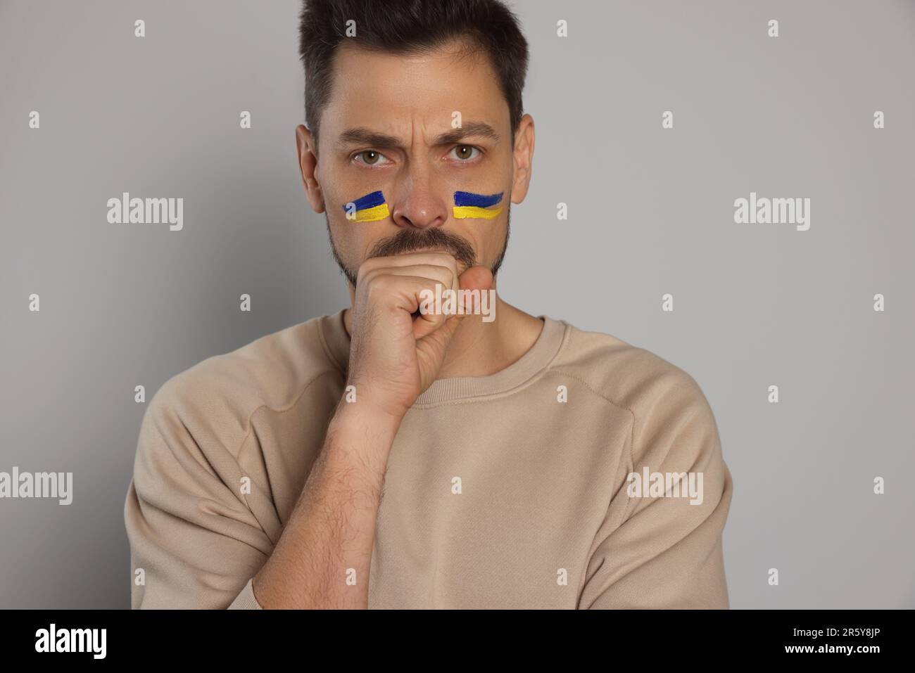 Angry man with drawings of Ukrainian flag on face against light grey ...