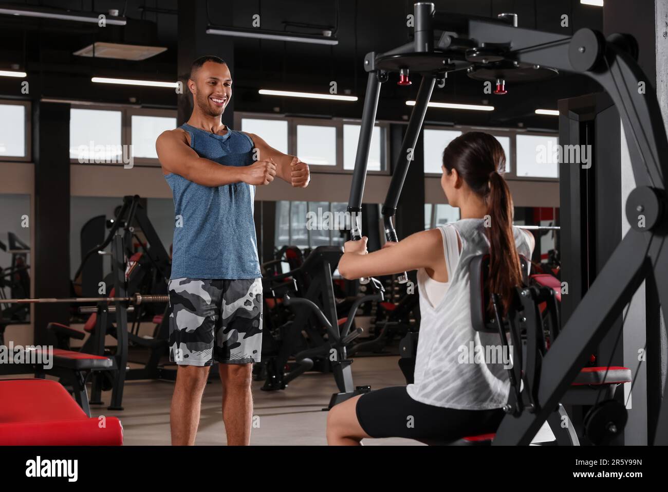 Happy trainer explaining woman how to do exercise properly in modern ...