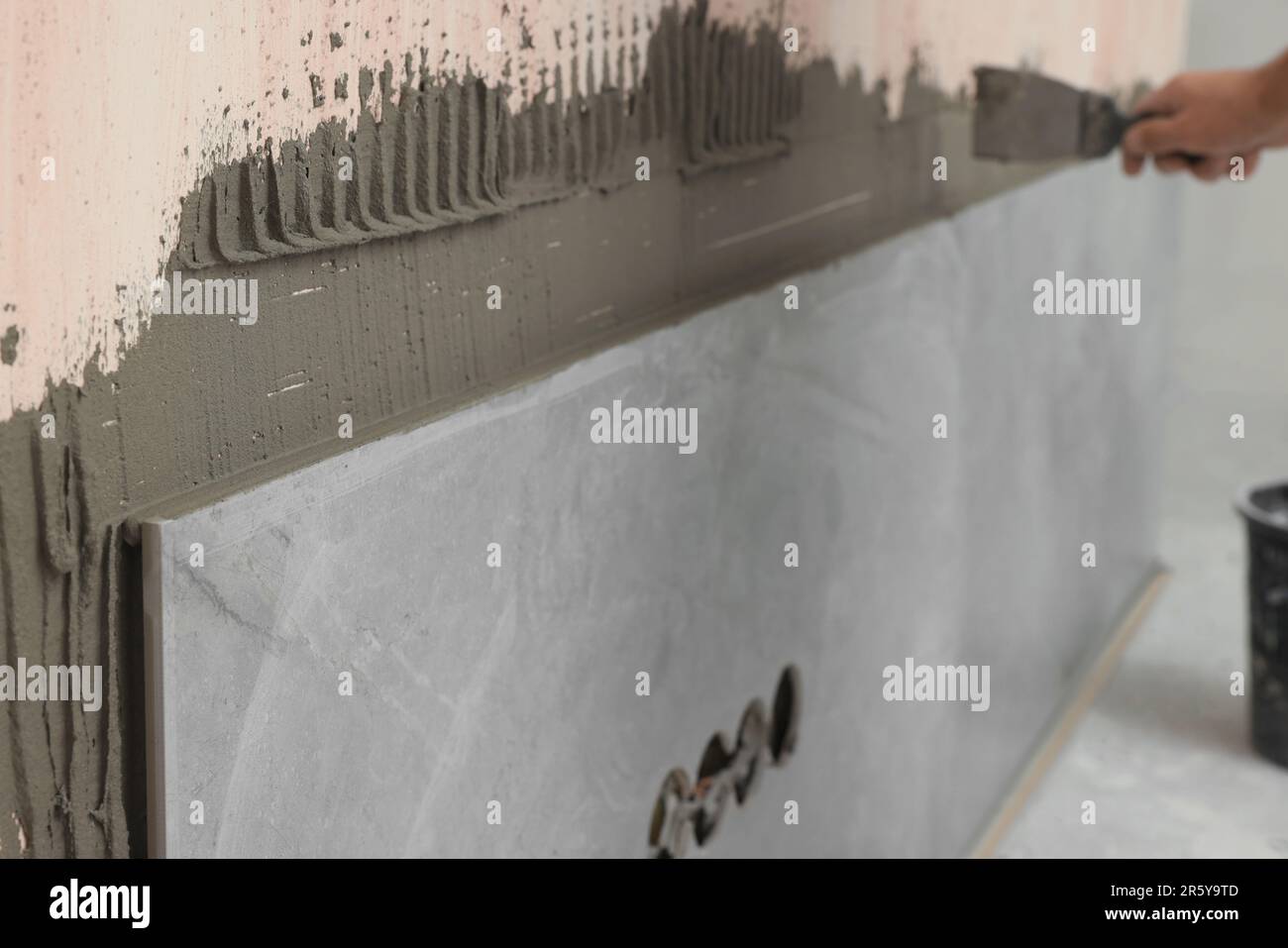 Worker spreading adhesive mix on wall, closeup. Tiles installation ...