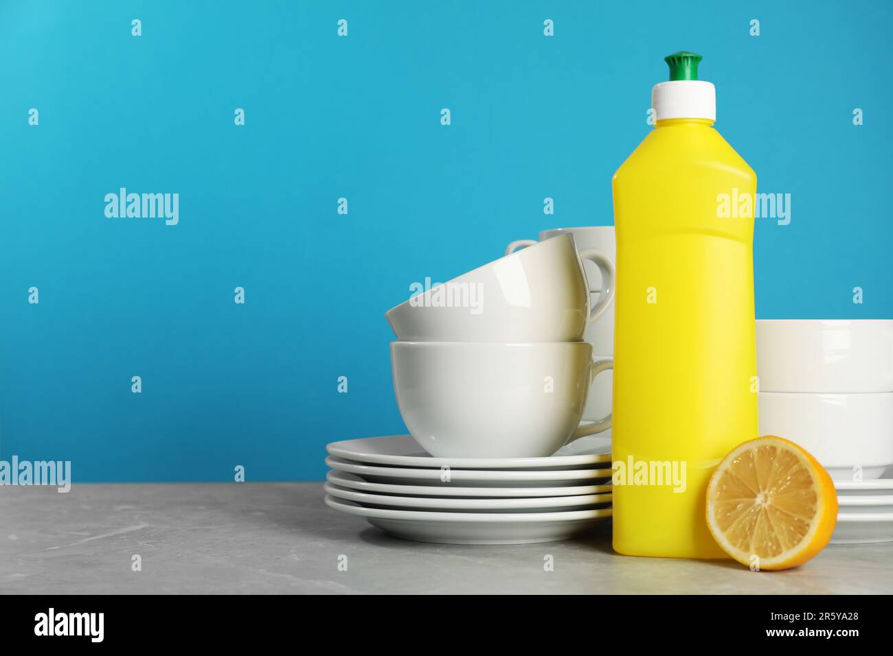 Clean tableware, dish detergent and lemon on grey table against light ...