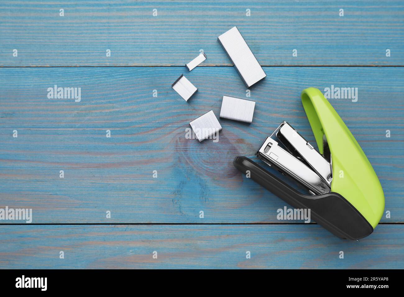New bright stapler with staples on light blue wooden table, fat lay ...