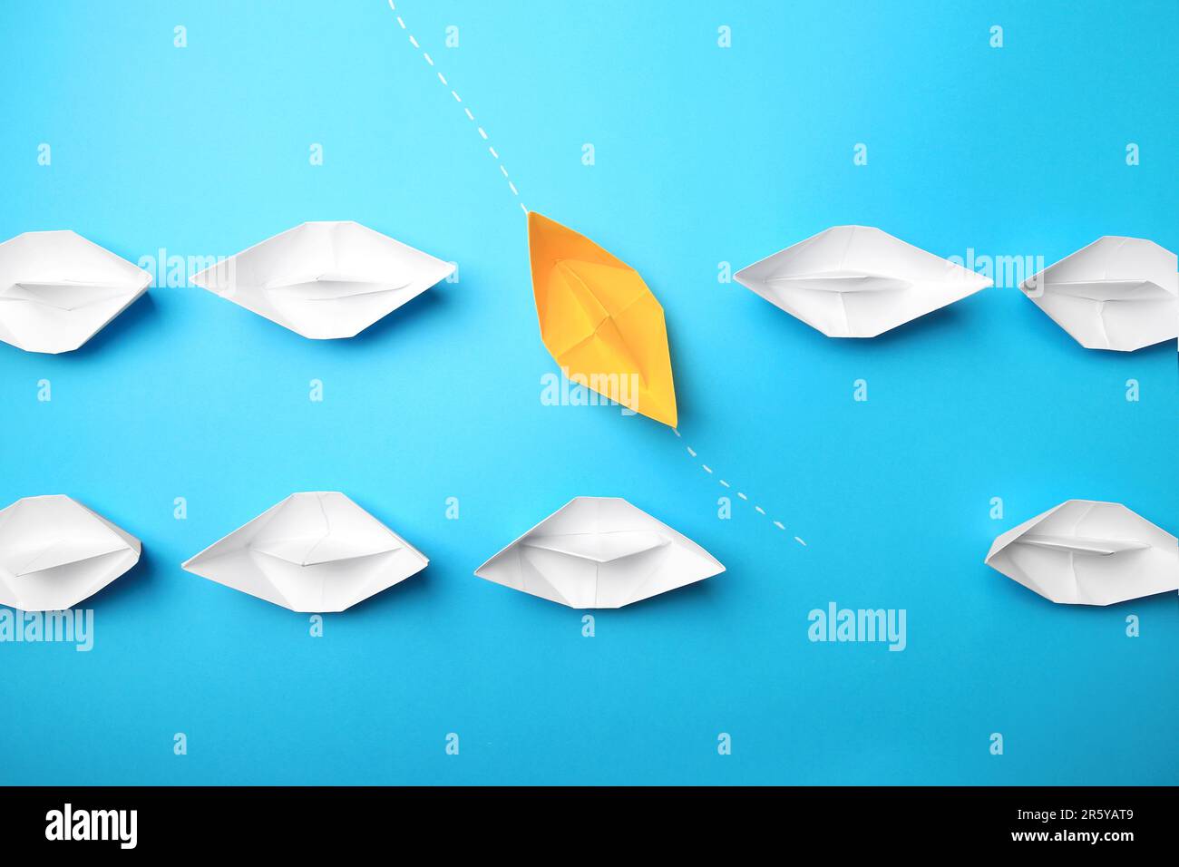 Yellow paper boat floating through others on light blue background ...