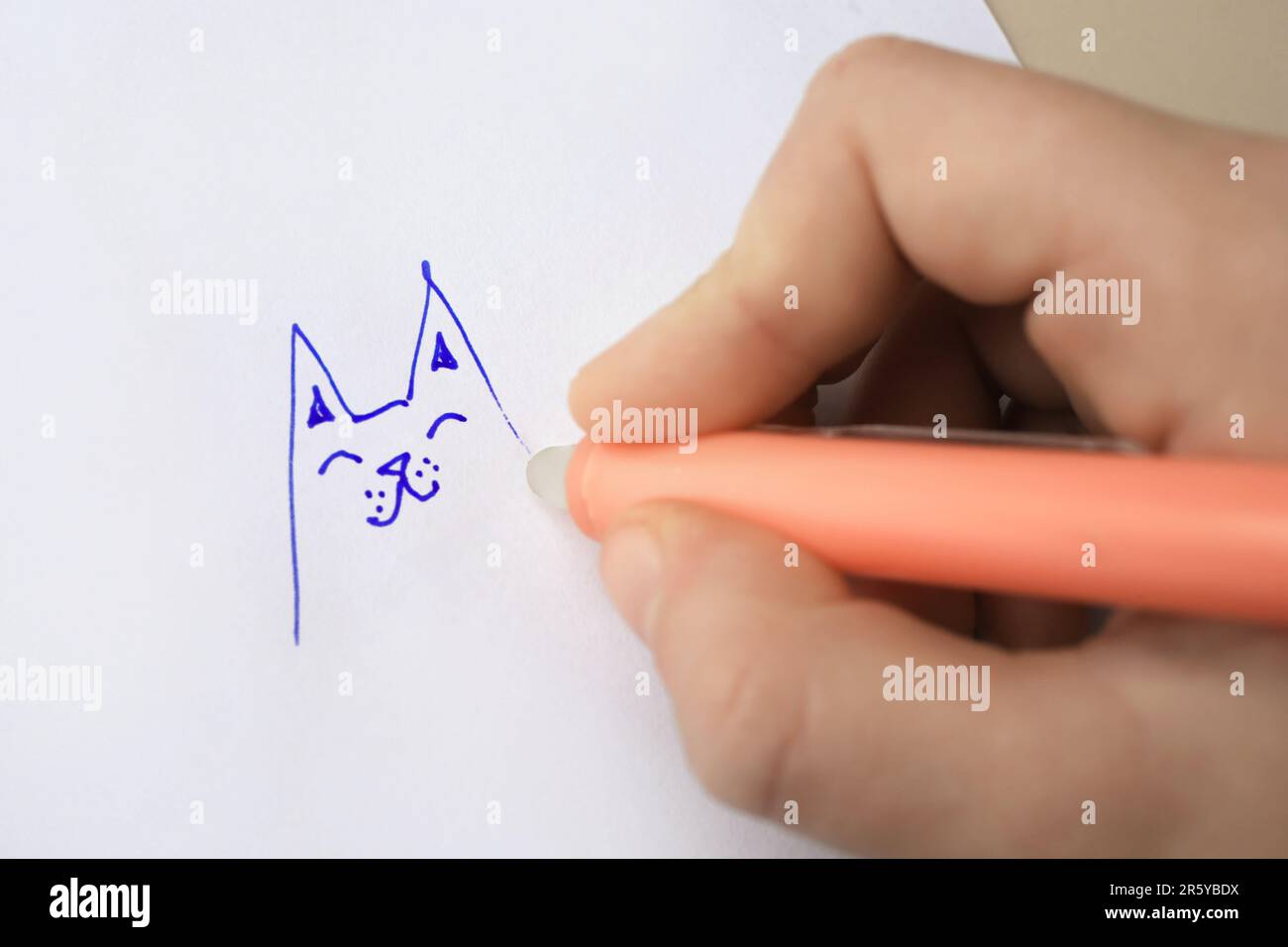 Child erasing drawing with erasable pen on paper sheet against beige ...