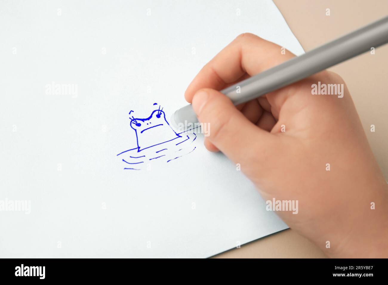 Child erasing drawing with erasable pen on paper sheet against beige ...
