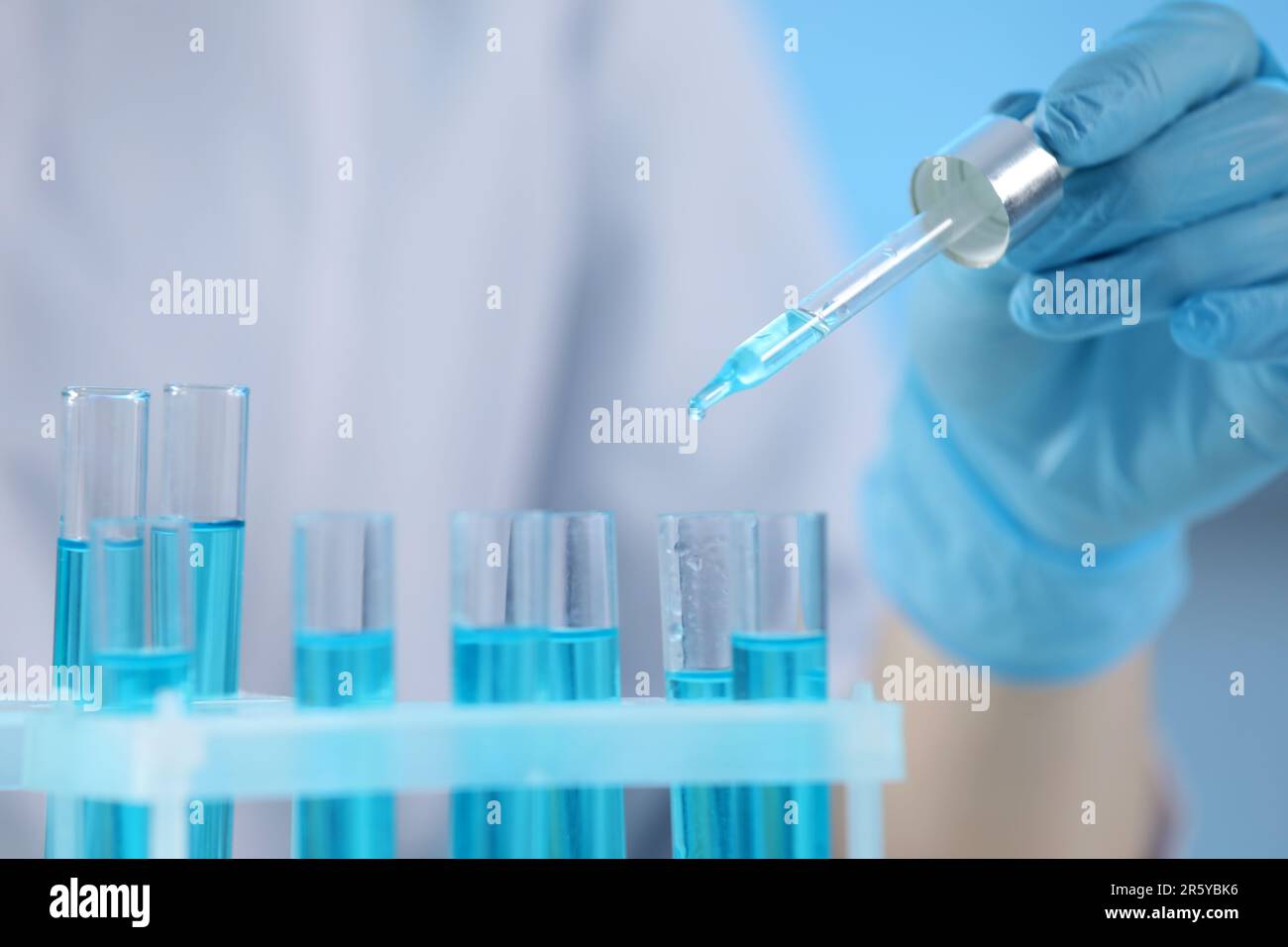 Scientist dripping liquid from pipette into test tube on blurred ...