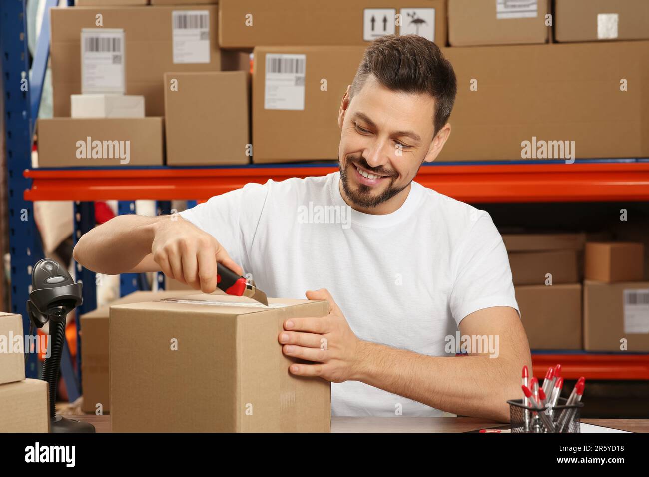 Post office worker with utility knife opening parcel indoors Stock ...