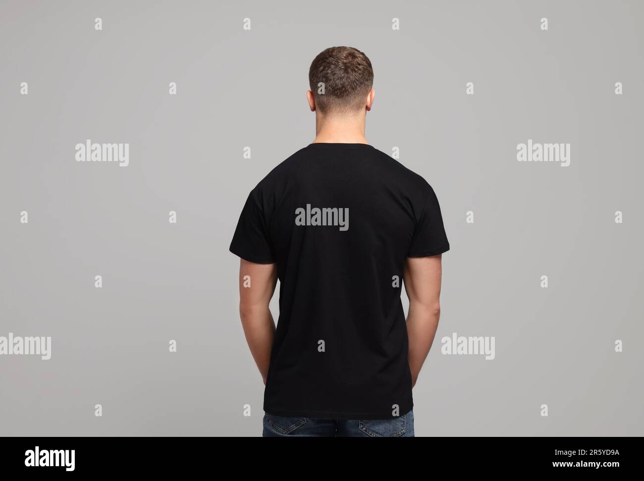 Man wearing black t-shirt on light grey background, back view. Mockup ...
