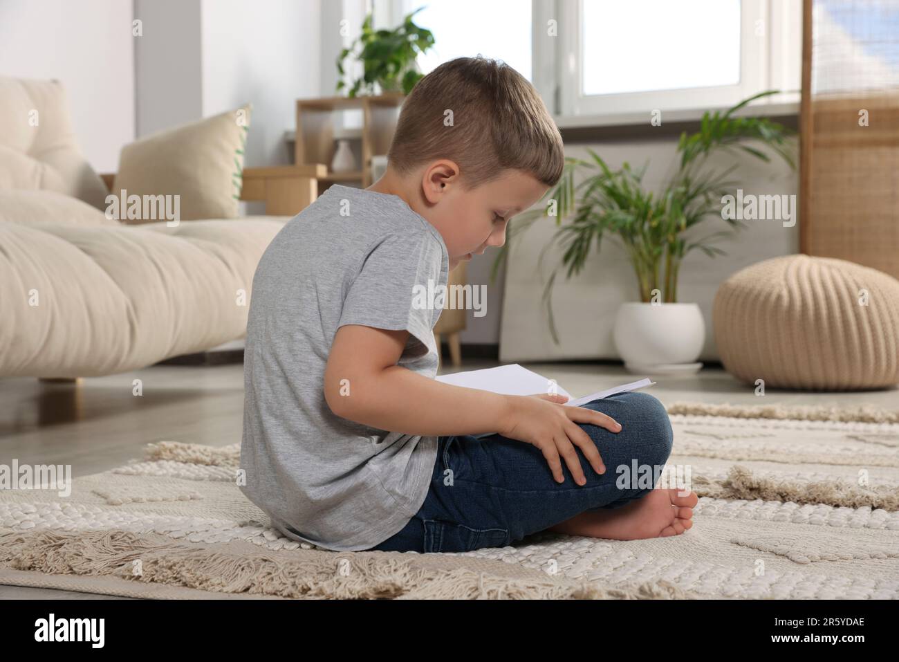 Boy with poor posture reading book on beige carpet in living room ...