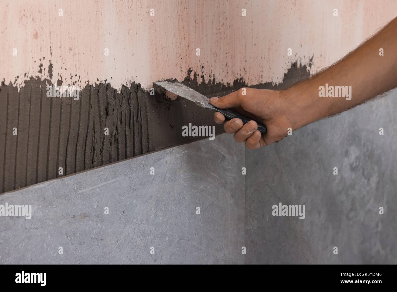 Worker spreading adhesive mix on wall, closeup. Tiles installation ...