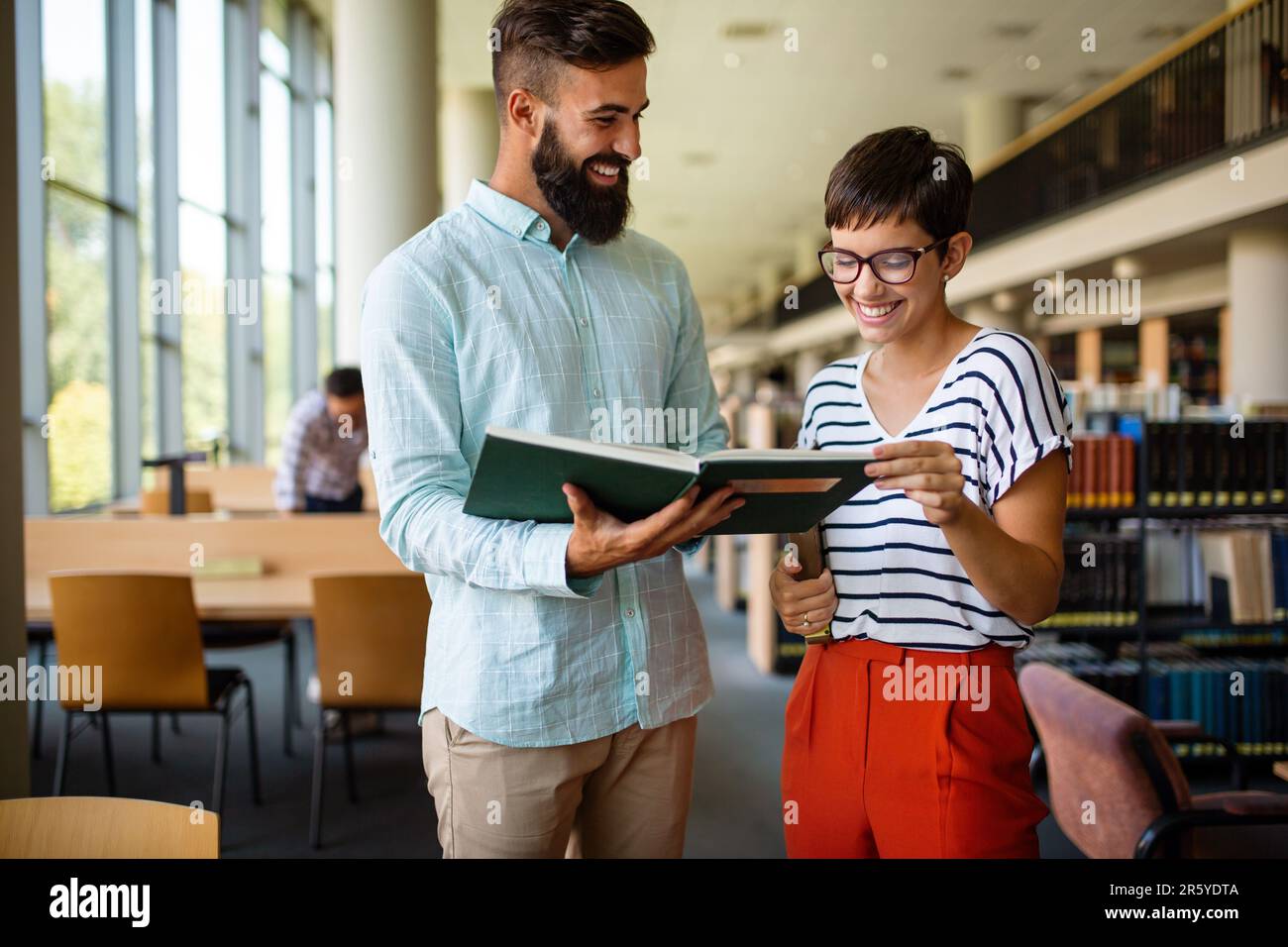 Happy university students studying with books in library. Group of ...
