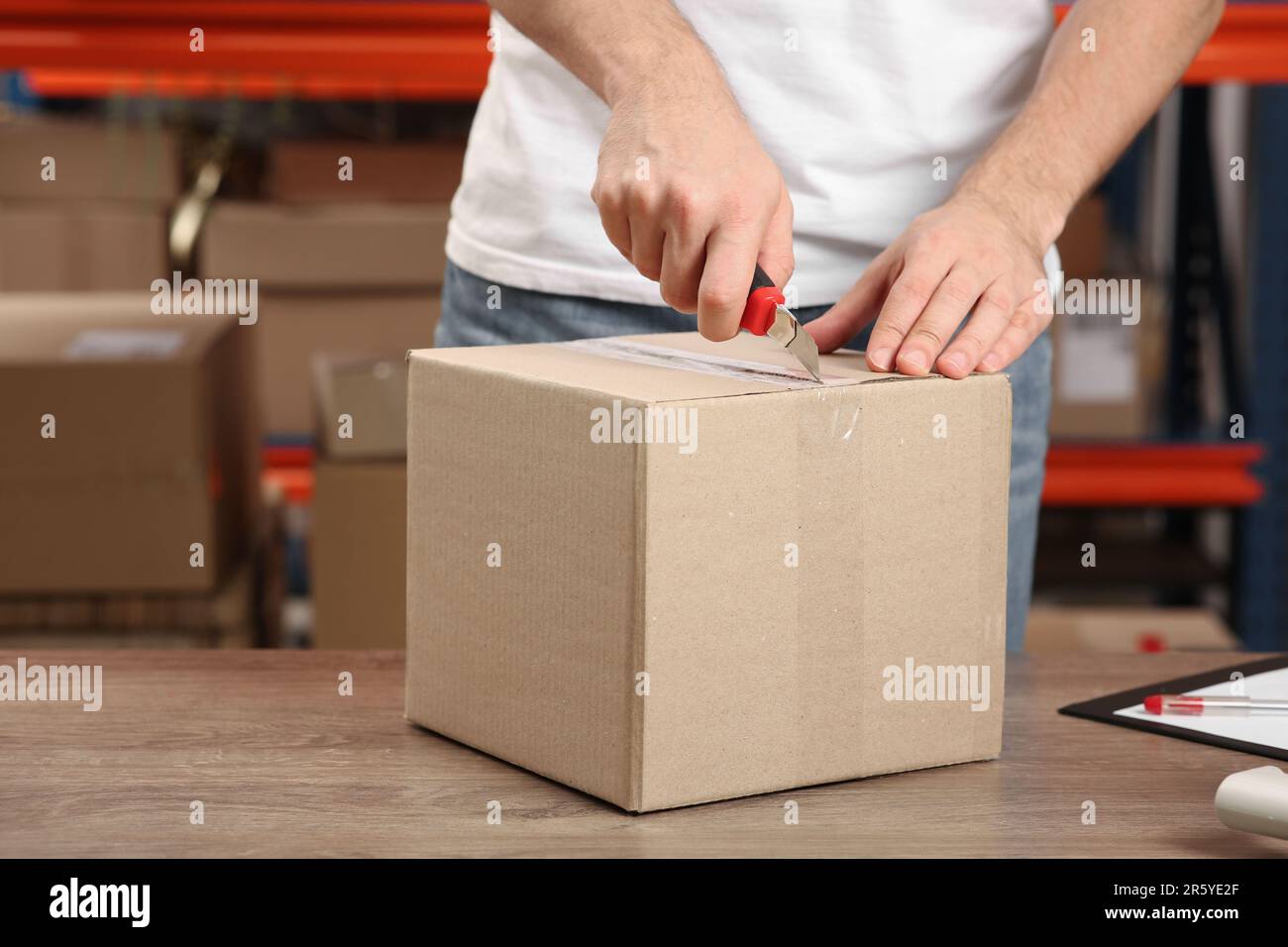 Post office worker with utility knife opening parcel at counter indoors ...