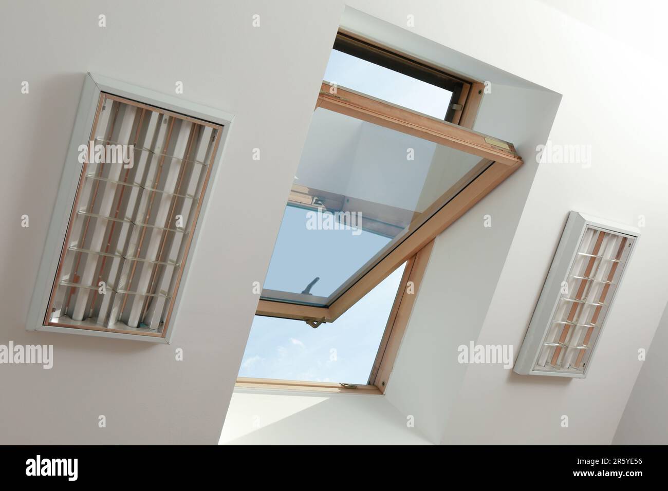 Open skylight roof window on slanted ceiling in attic room, bottom view ...