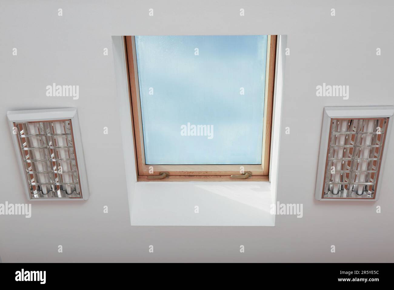 Skylight roof window and lamps on slanted ceiling in attic room, bottom ...