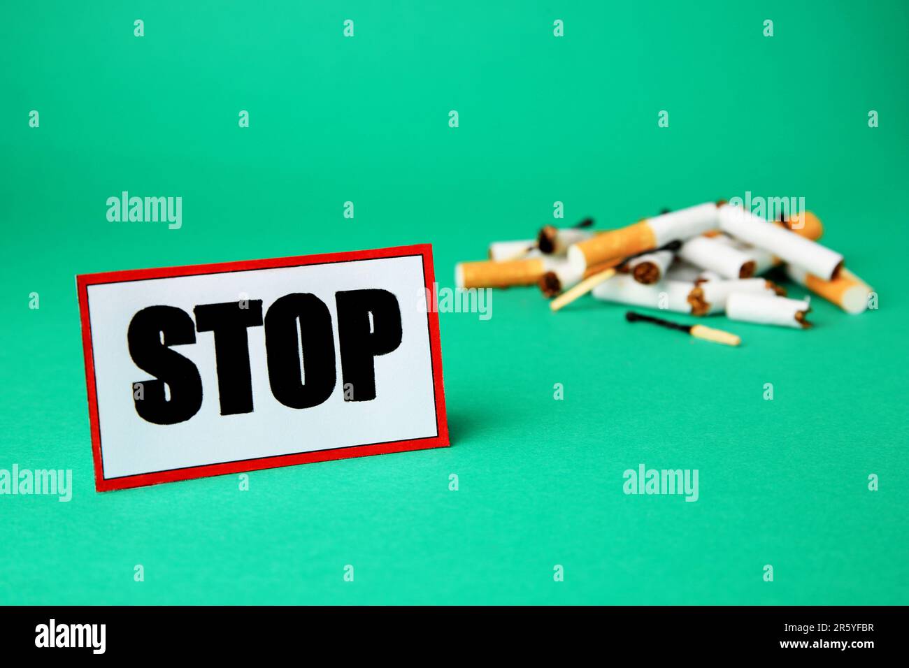 Card with word Stop near pile of cigarette stubs and burnt matches on ...