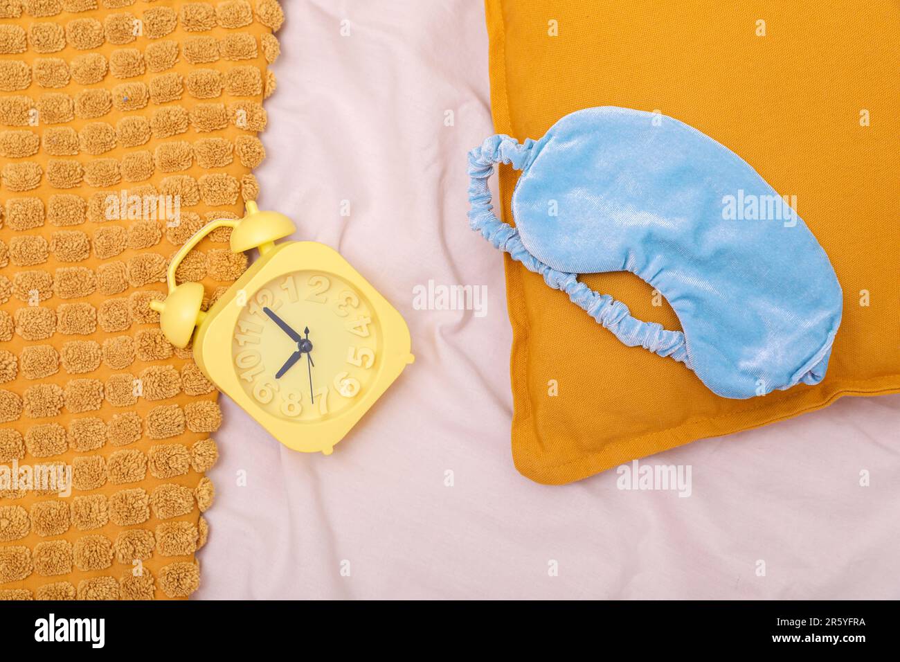 Light blue sleep mask, pillow and alarm clock on beige cloth, flat lay ...