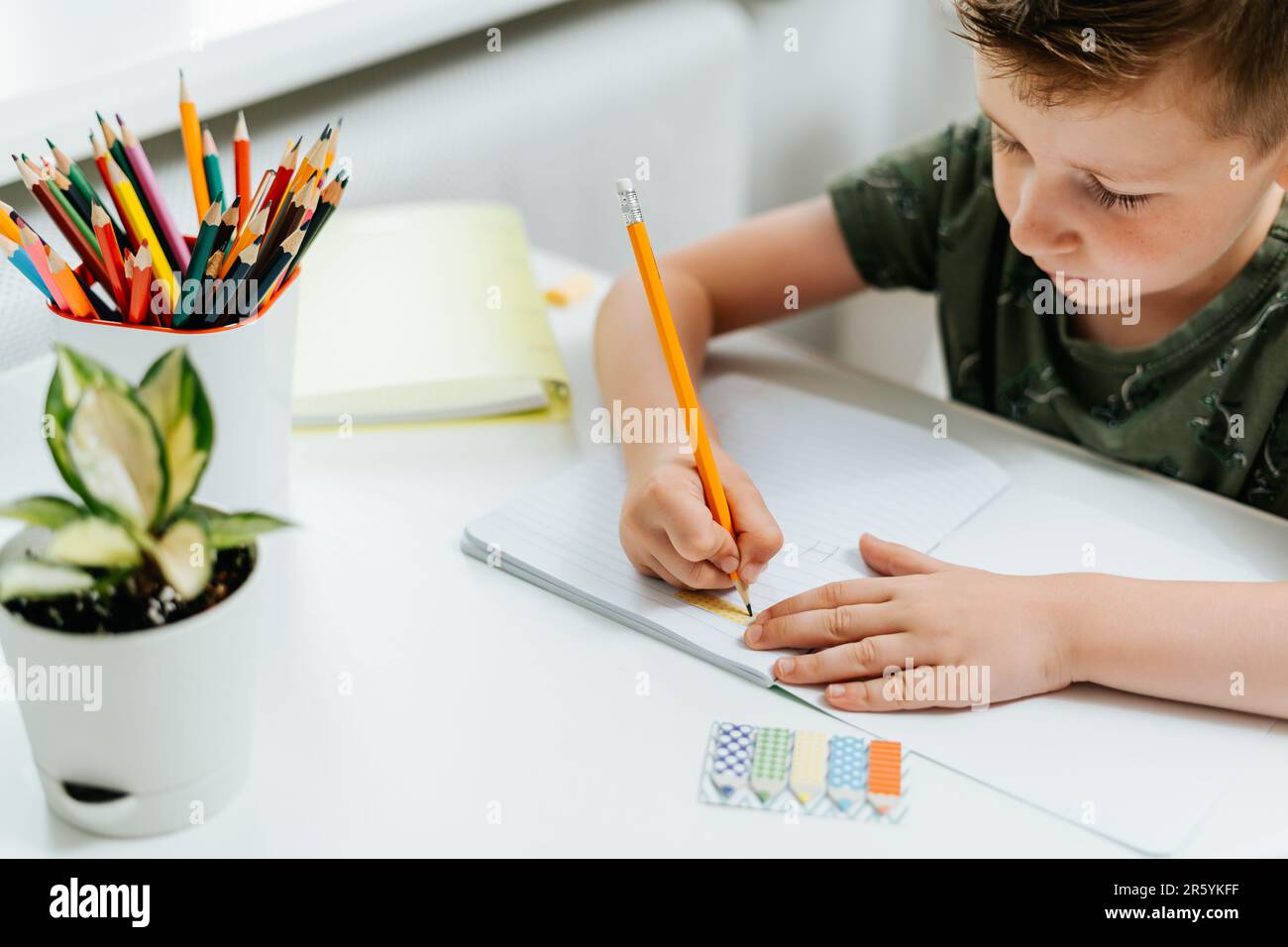 School kid boy studying at home with book, draw in notepad and doing ...