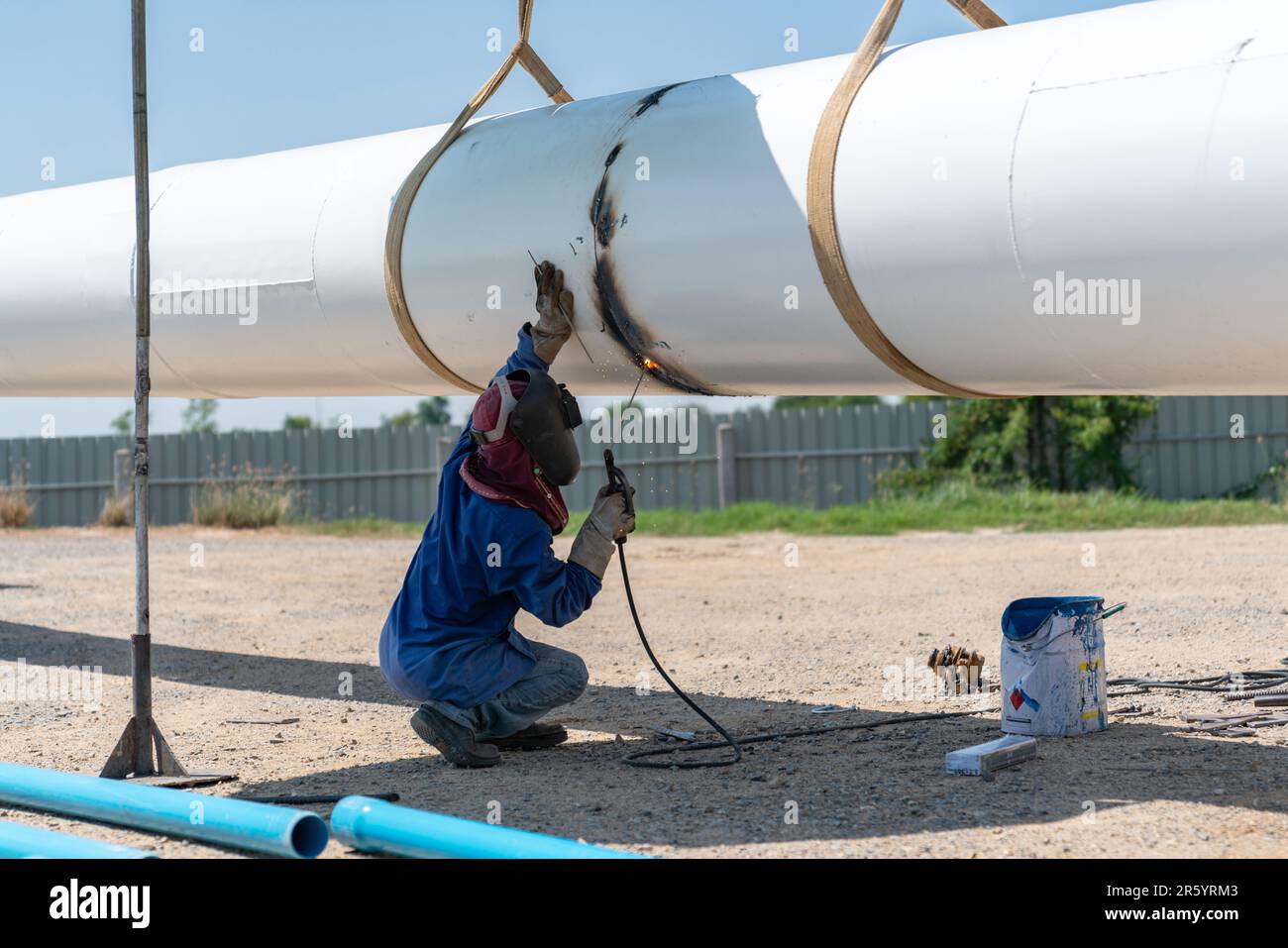 Worker in protective suit and mask crouching and welding pipe of water ...