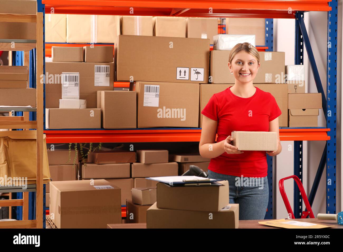 Post office worker with parcel near rack indoors Stock Photo - Alamy