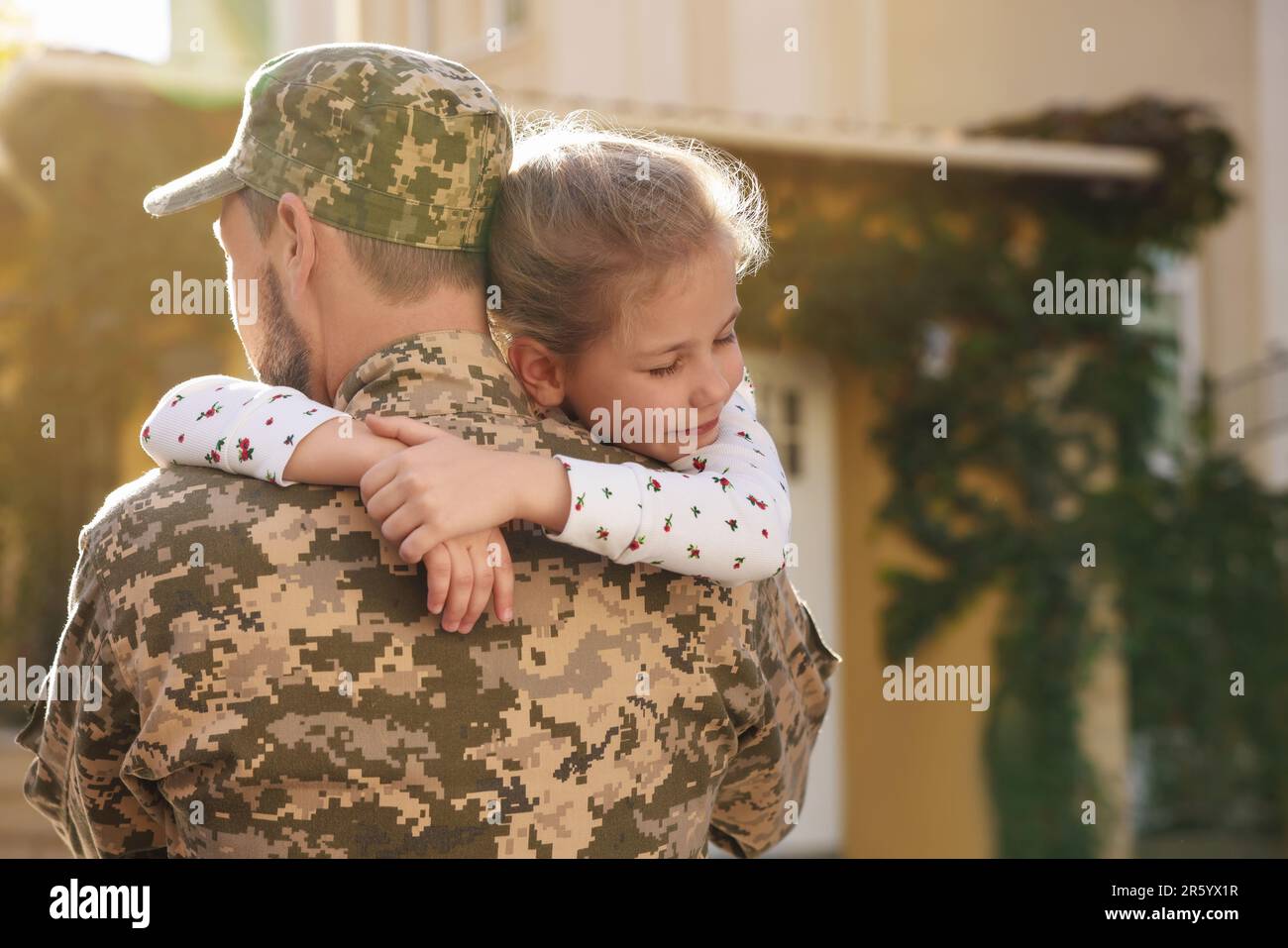 Soldier in Ukrainian military uniform hugging his daughter outdoors ...