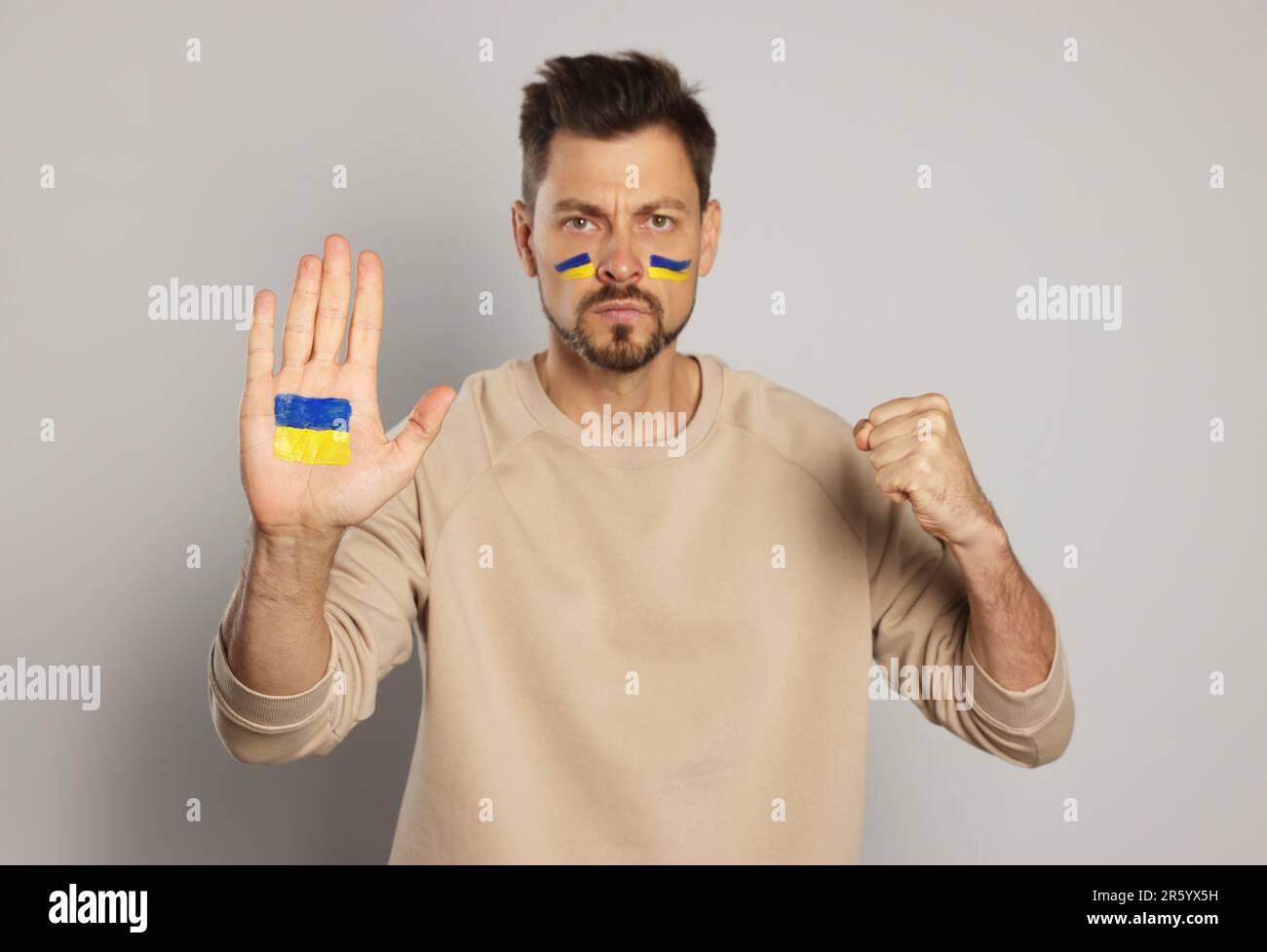 Angry man with drawings of Ukrainian flag against light grey background ...
