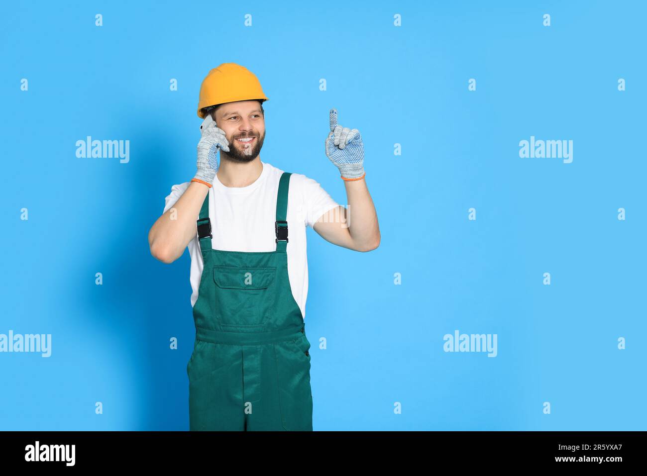 Professional repairman in uniform talking on smartphone against light ...