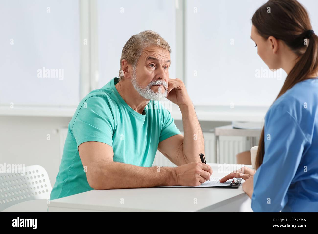 Doctor helping patient filling his medical card at table in clinic ...