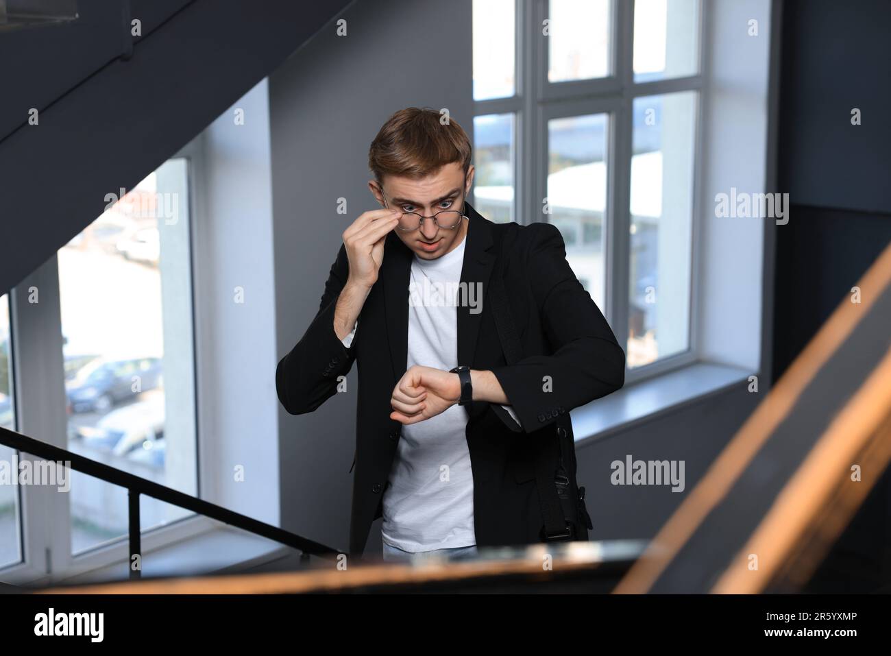 Emotional young man checking time in office. Being late Stock Photo - Alamy