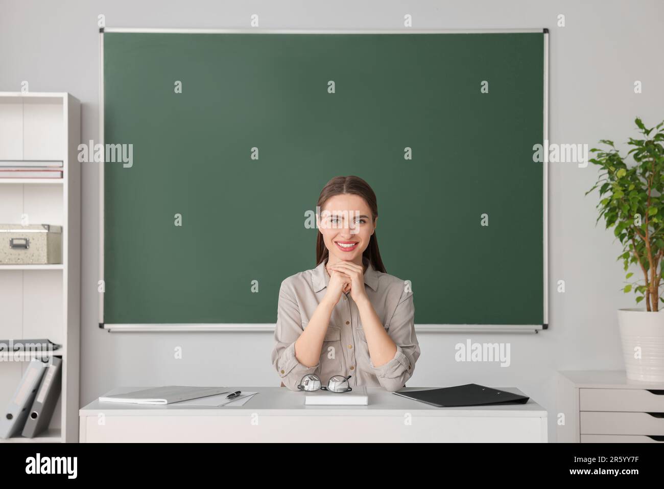 Portrait of beautiful young teacher at table in classroom Stock Photo ...