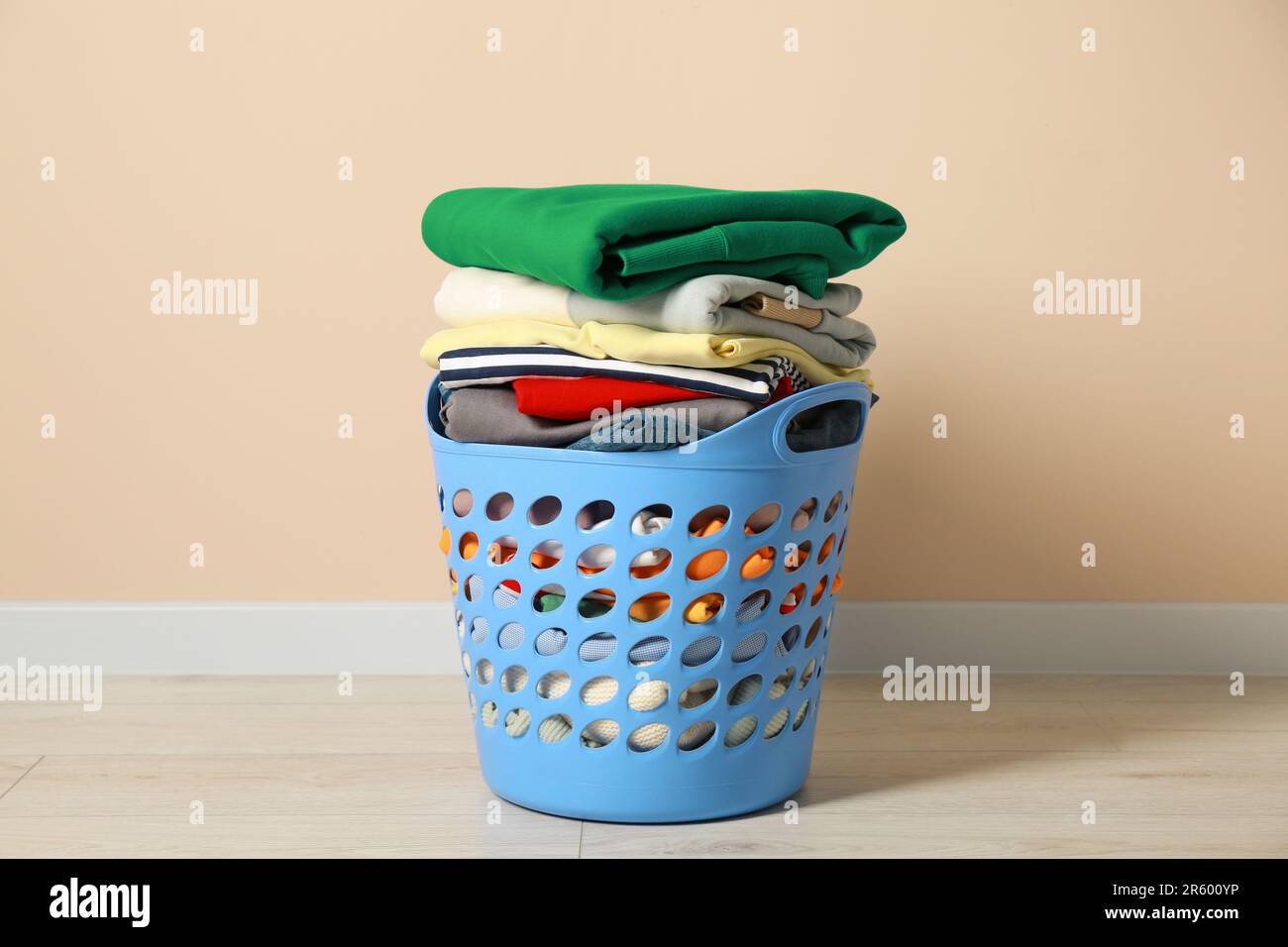 Plastic laundry basket with clean clothes on floor near beige wall ...